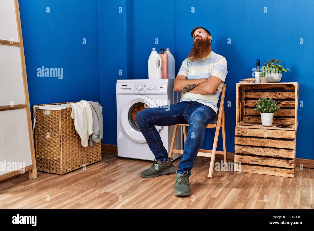 Young redhead man tired waiting for washing machine at laundry room ...