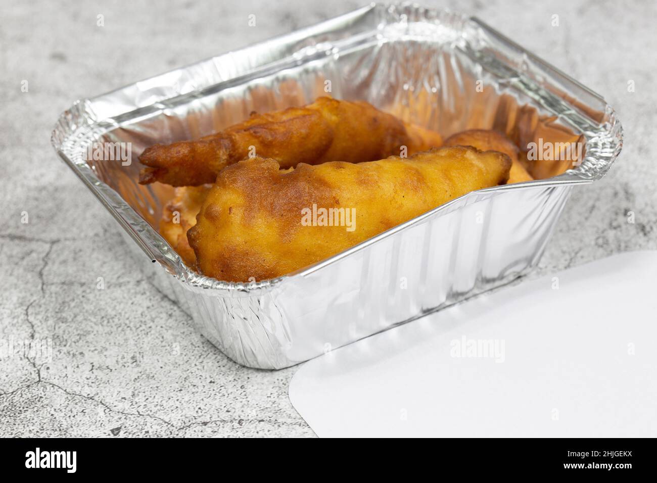 Battered chicken portions in a foil takeaway tray with lid. On a ...