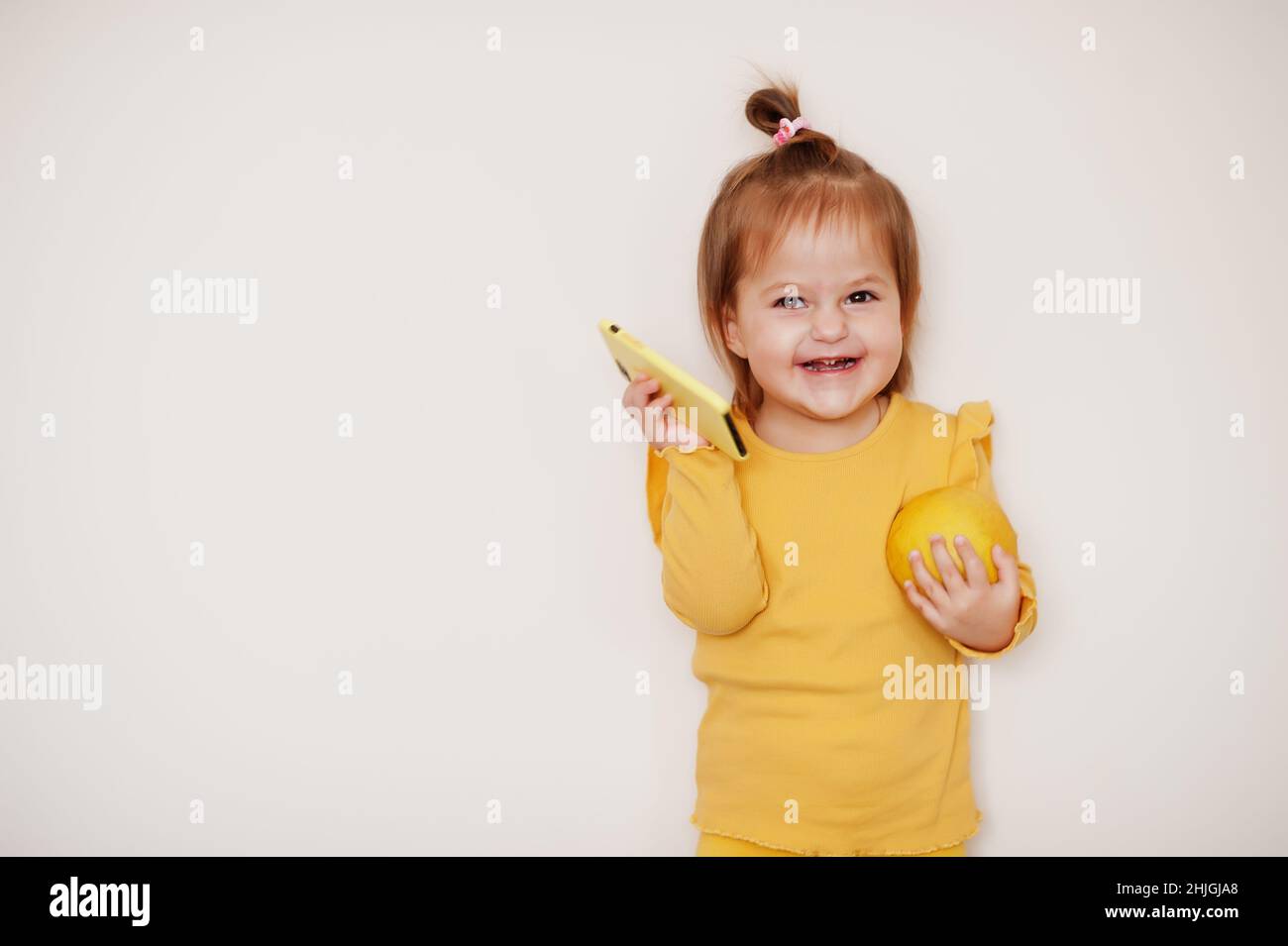 Baby girl in yellow with lemon and mobile phone, isolated background ...