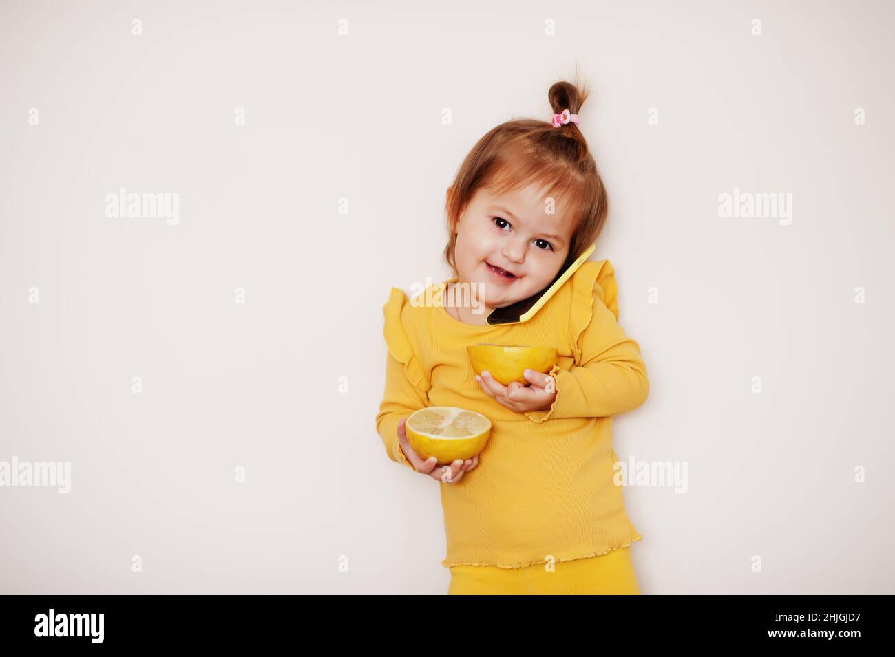 Baby girl in yellow with lemon and mobile phone, isolated background ...