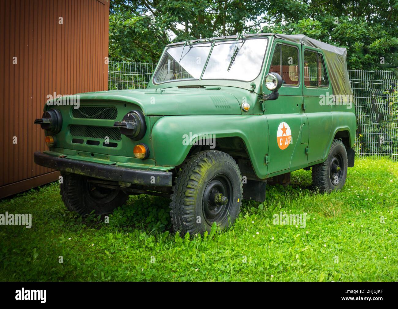 an old russian military jeep stands next to a house wall in the grass ...