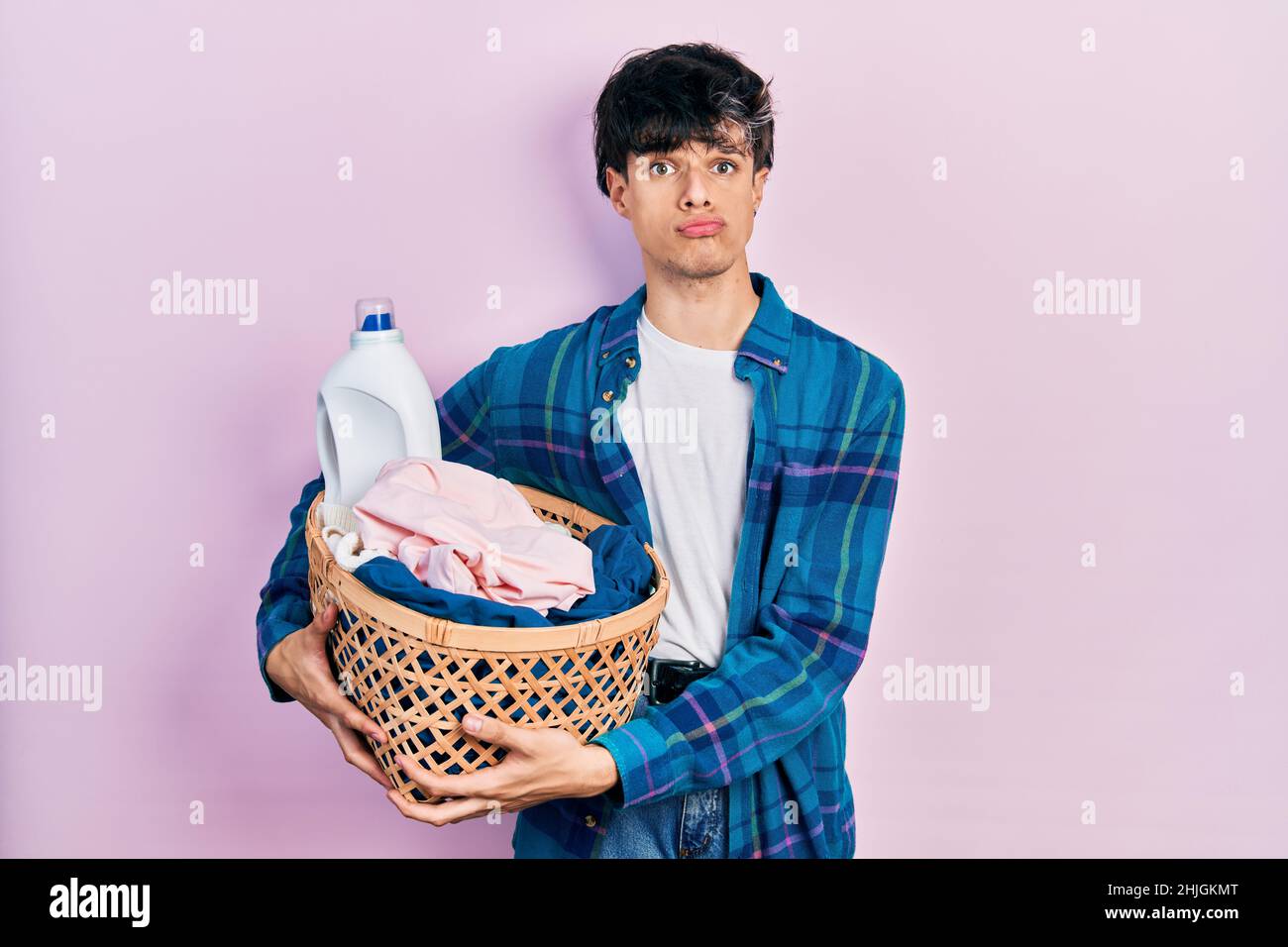 Handsome hipster young man holding laundry basket and detergent bottle ...