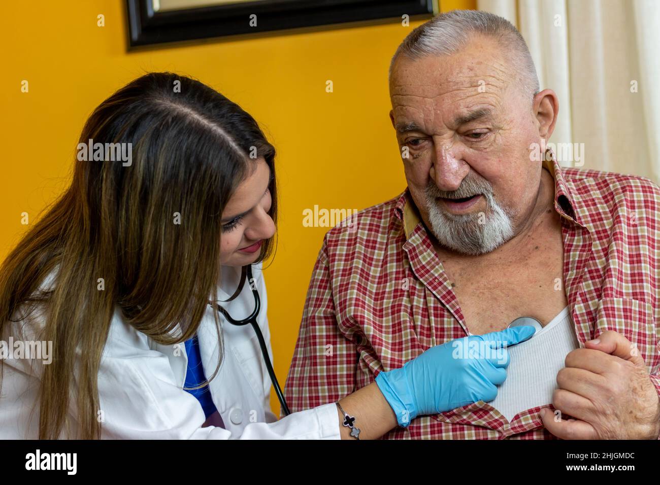 Female doctor listening to chest of senior male patient during medical ...