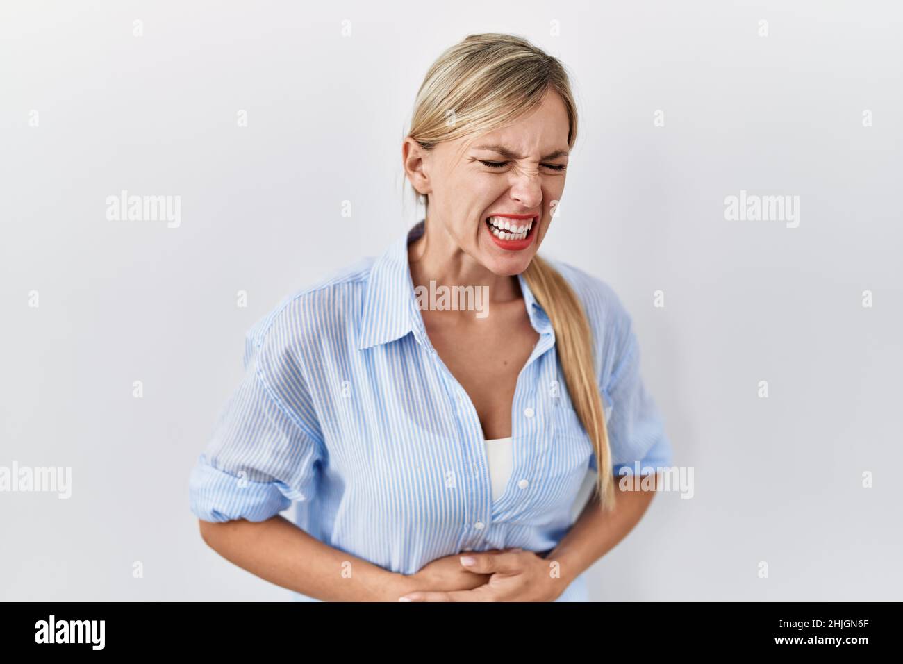 Beautiful blonde woman standing over white background with hand on ...