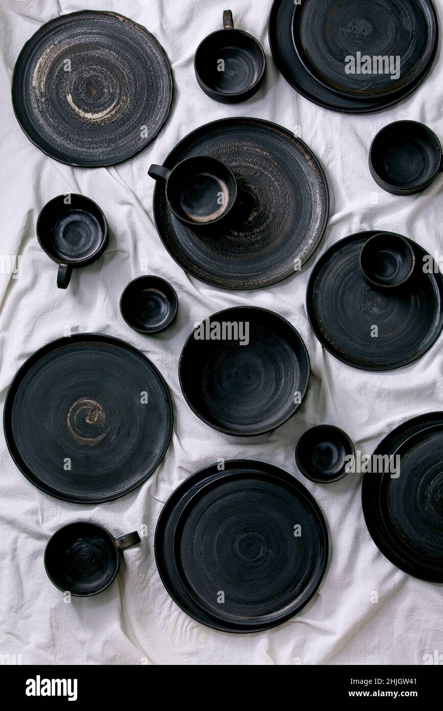 Set of empty black handcrafted ceramic plates, bowls and cups on white ...
