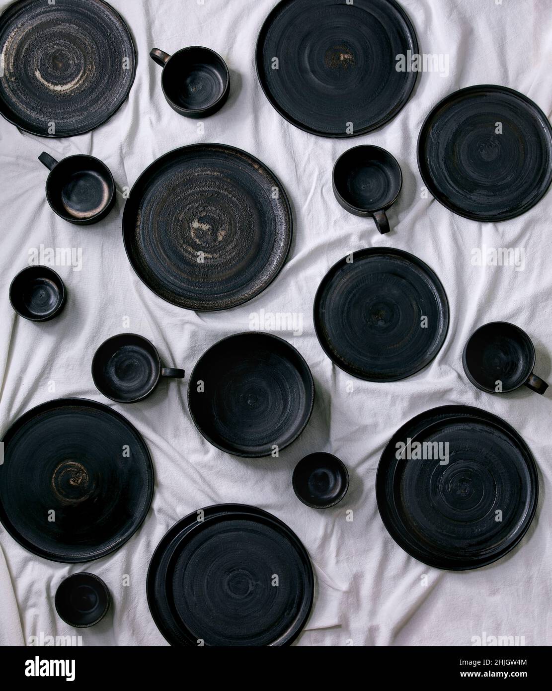 Set of empty black ceramic plates, bowls and cups on white linen table ...