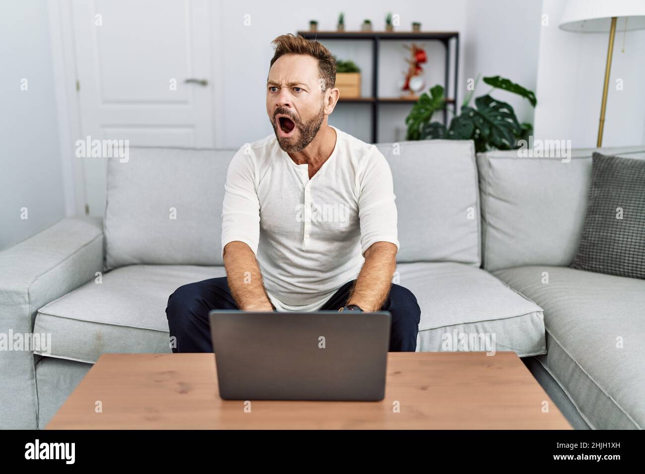 Middle age man using laptop at home angry and mad screaming frustrated ...