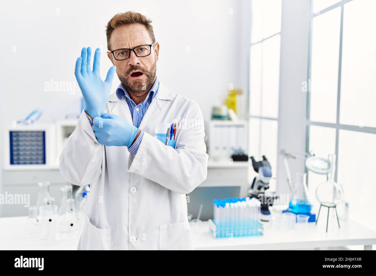 Middle age man working at scientist laboratory in shock face, looking ...