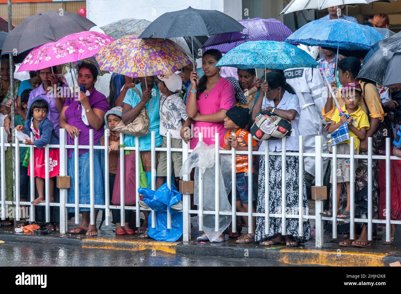 A crowd of people shelter under umbrellas from the rain as they wait ...