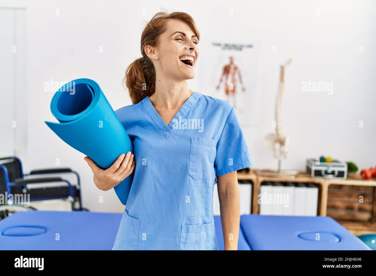 Young caucasian physio therapist girl smiling happy holding yoga mat at ...