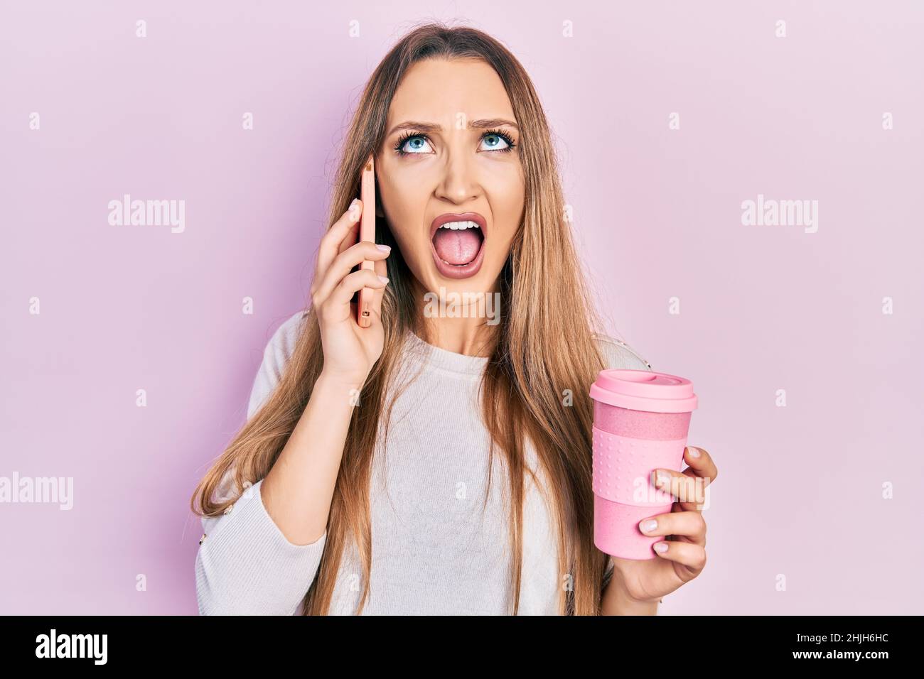 Young blonde girl using smartphone and drinking a cup of coffee angry ...