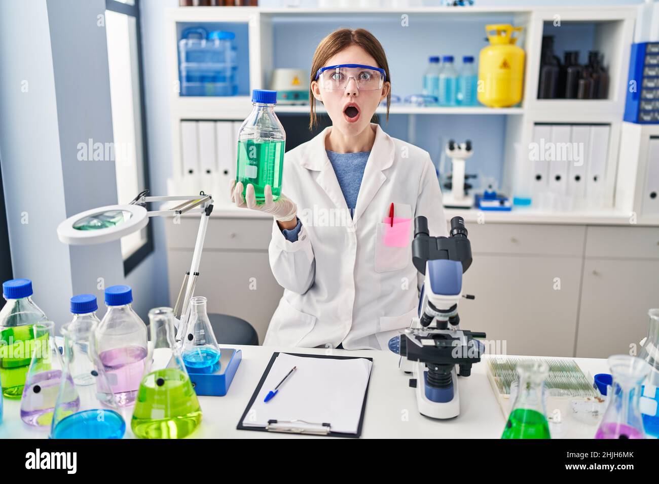 Young brunette woman working at scientist laboratory scared and amazed ...