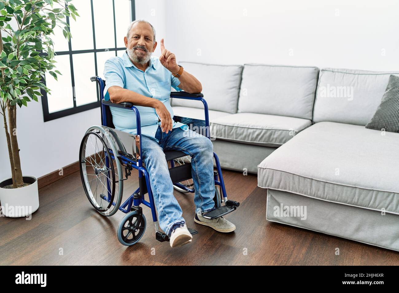 Handsome senior man sitting on wheelchair at the living room showing ...