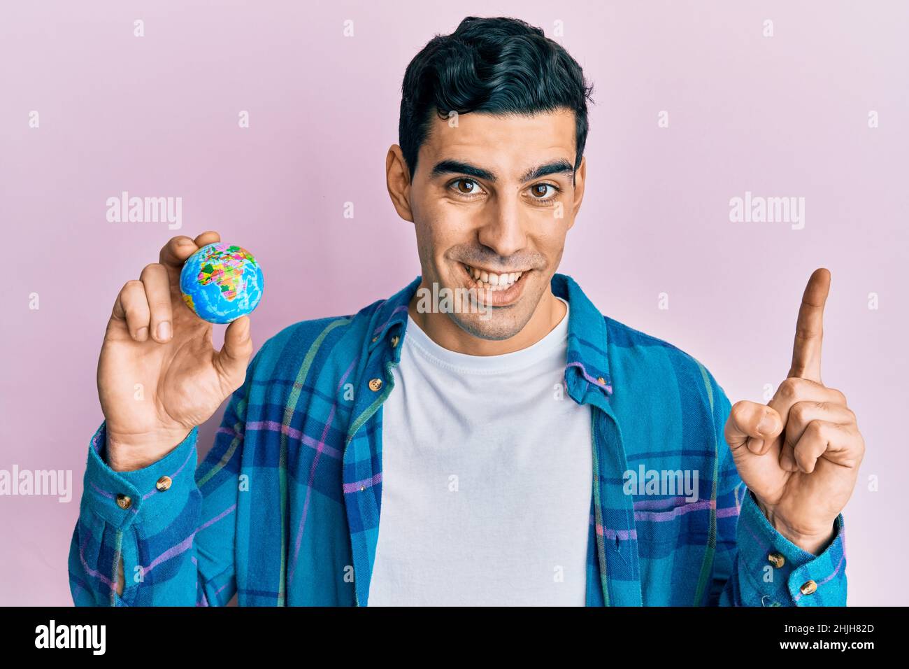 Handsome hispanic man holding small world ball surprised with an idea ...