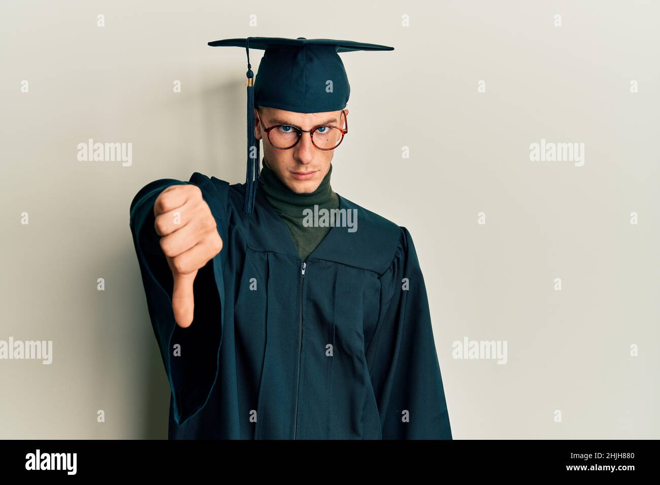 Young caucasian man wearing graduation cap and ceremony robe looking ...