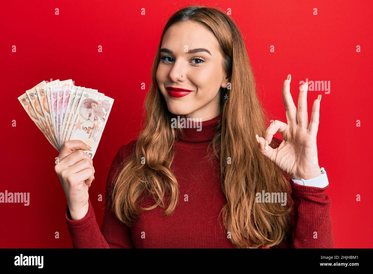 Young blonde woman holding turkish lira banknotes doing ok sign with ...