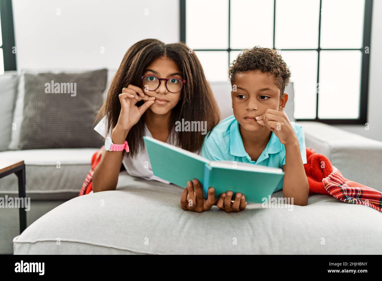 Two siblings lying on the sofa reading a book mouth and lips shut as ...