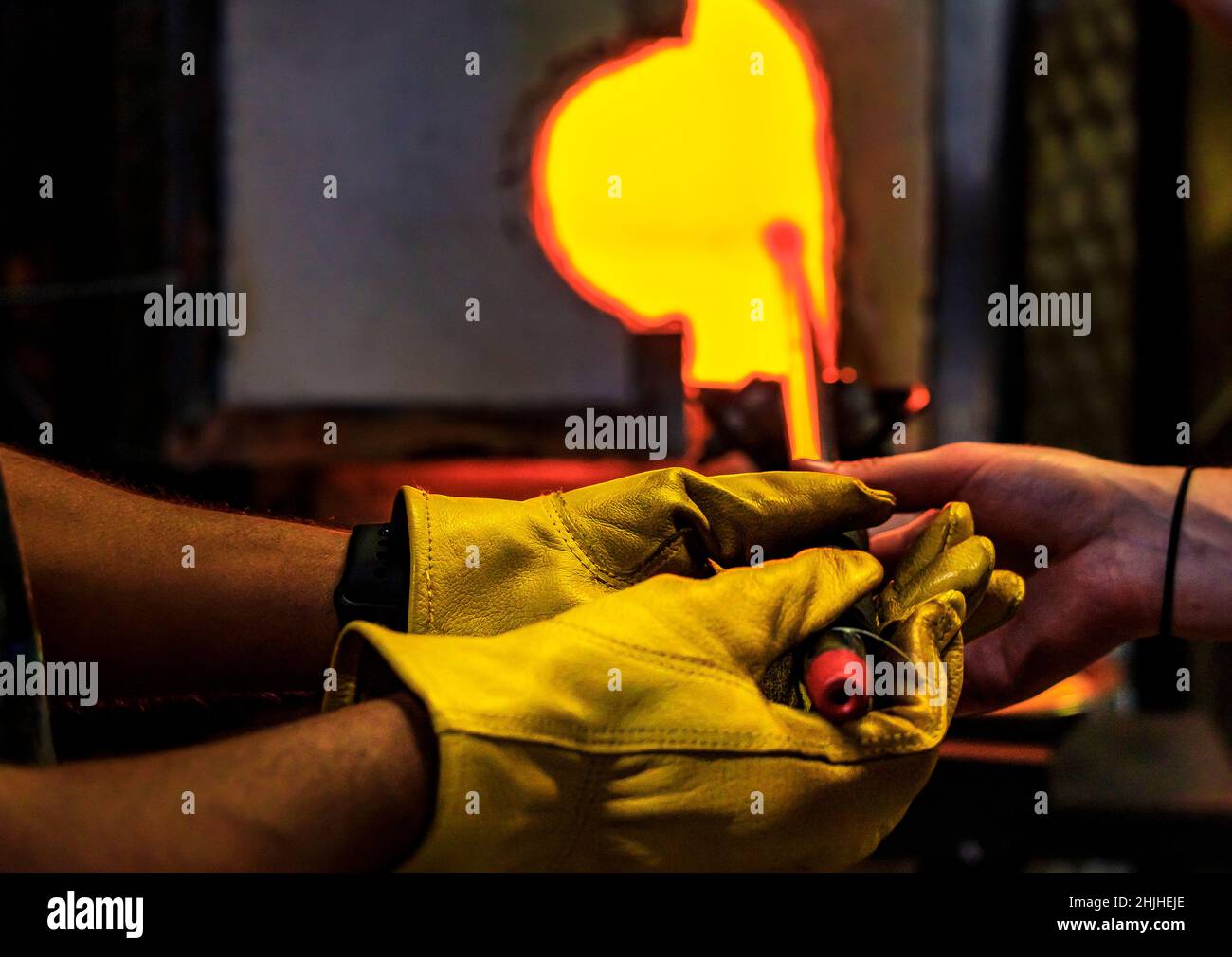 Glass blower shaping a bubble of melted glass on a rod in the furnace ...