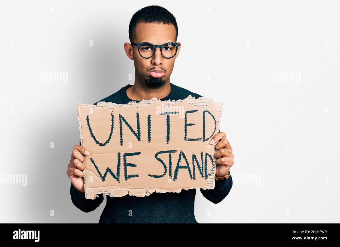 Young african american man holding united we stand banner depressed and ...