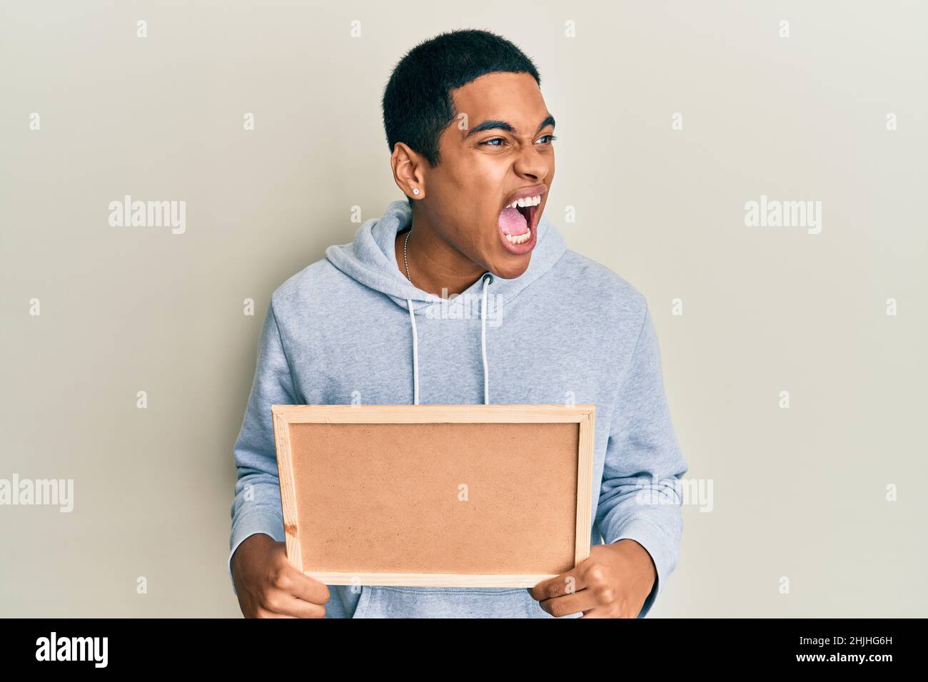 Young handsome hispanic man holding empty corkboard angry and mad ...