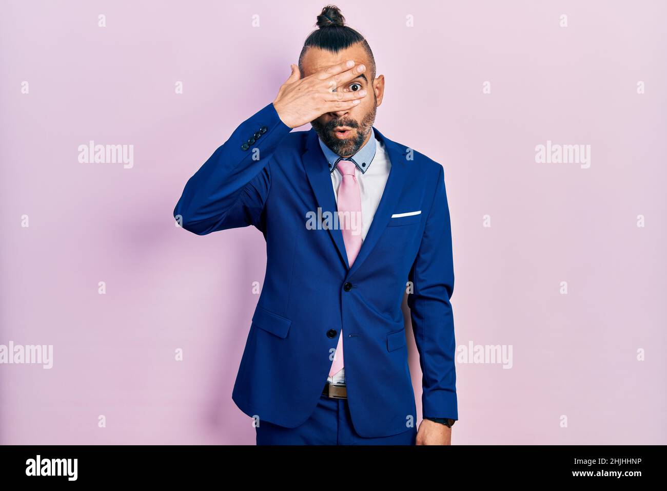 Young hispanic man wearing business suit and tie peeking in shock ...