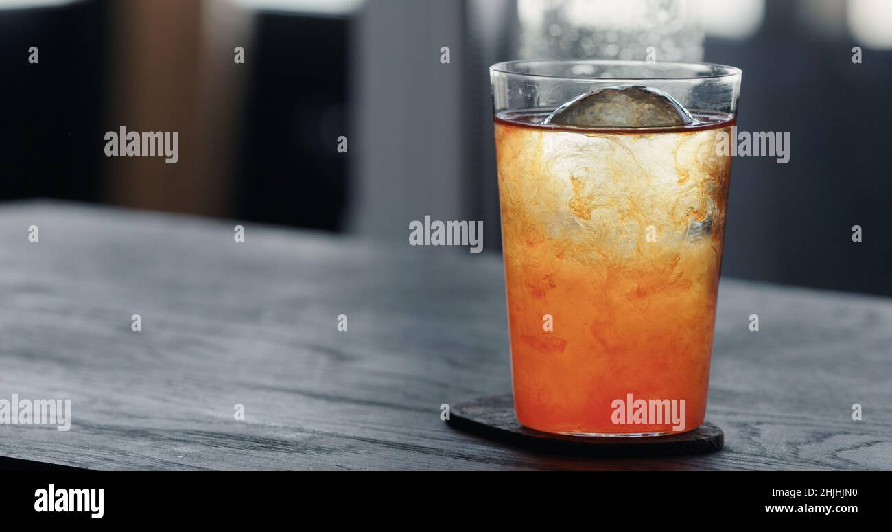 pour tonic water over clear ice ball in tumbler glass on black oak ...