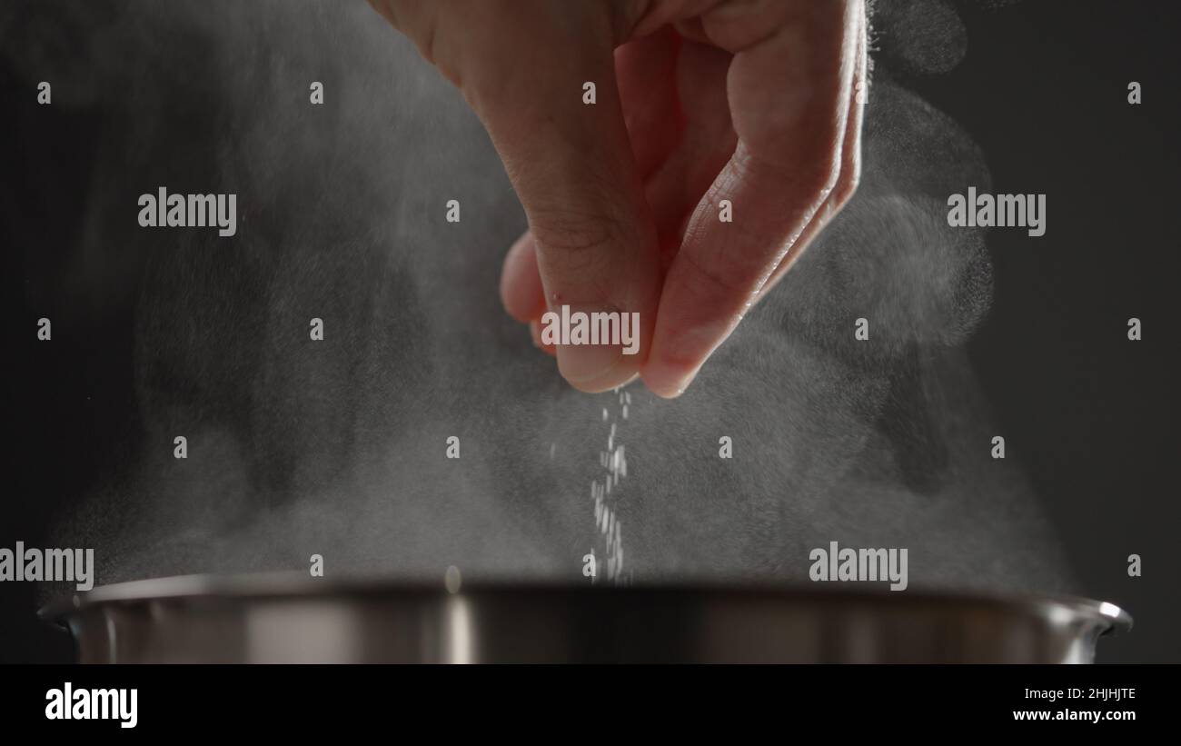 man adding salt to boiling water in saucepan with strong backlight ...