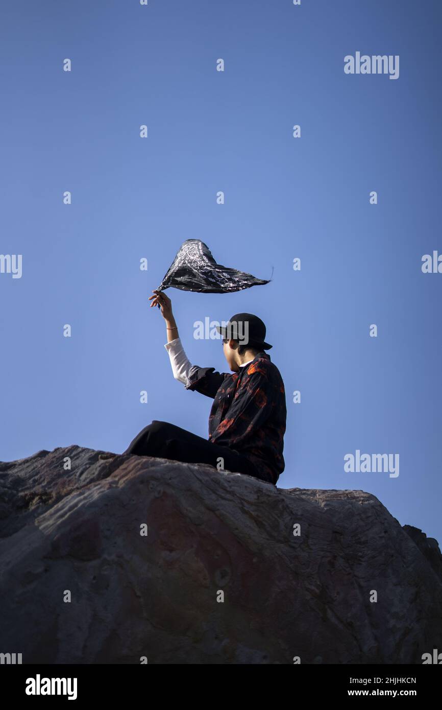 Vertical of an Indian female holding a handkerchief sitting on a rock ...