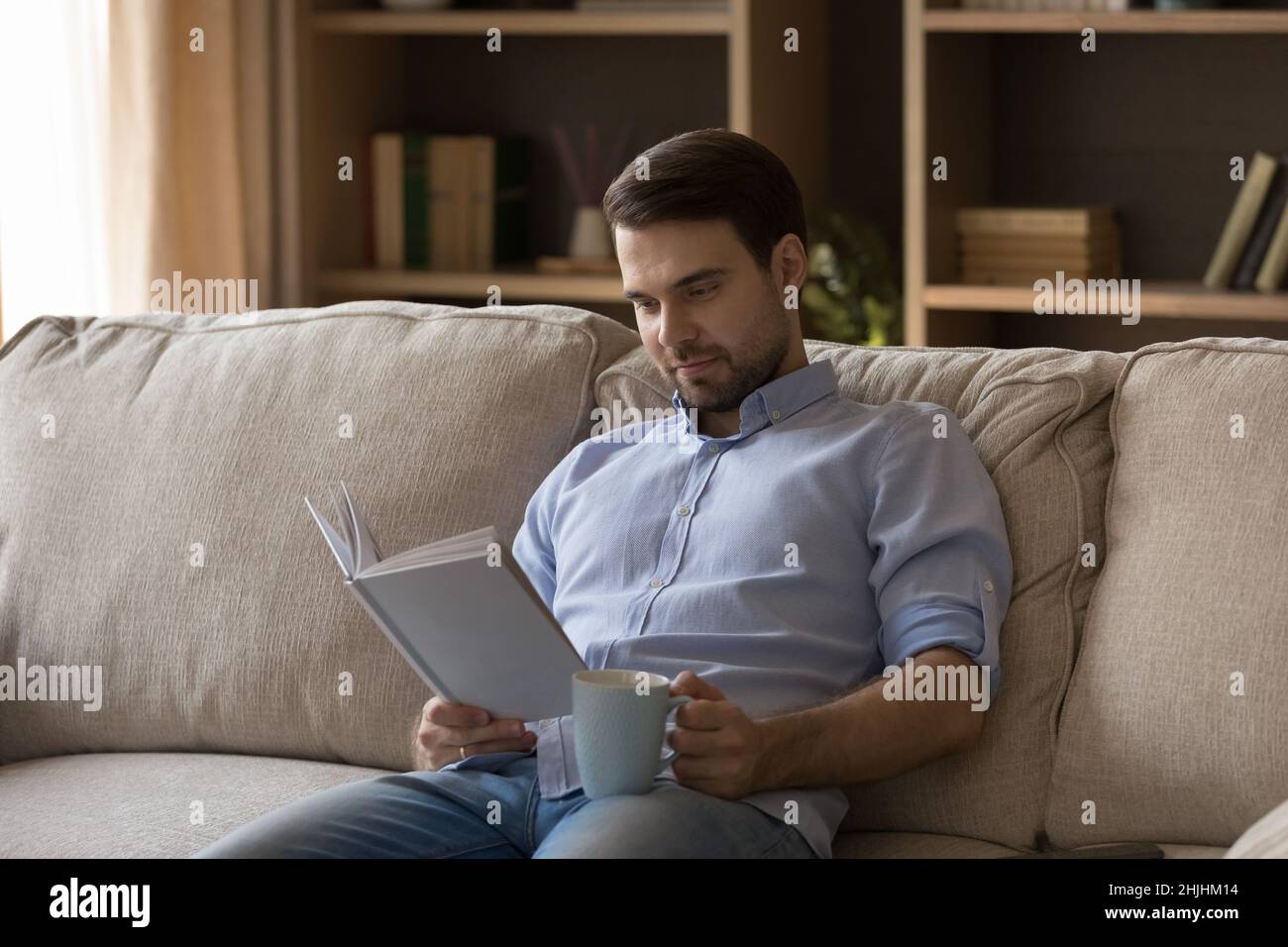Smiling relaxed young man involved in reading paper book Stock Photo ...