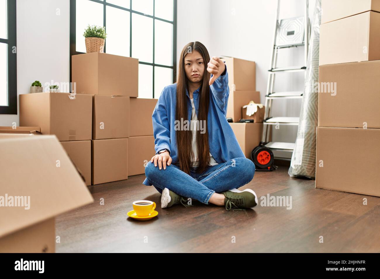 Young Chinese Girl Sitting On The Floor At New Home Looking Unhappy And