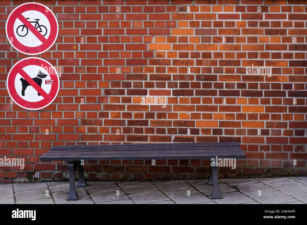A wooden bench in front of a brick wall. Red prohibition signs forbid ...
