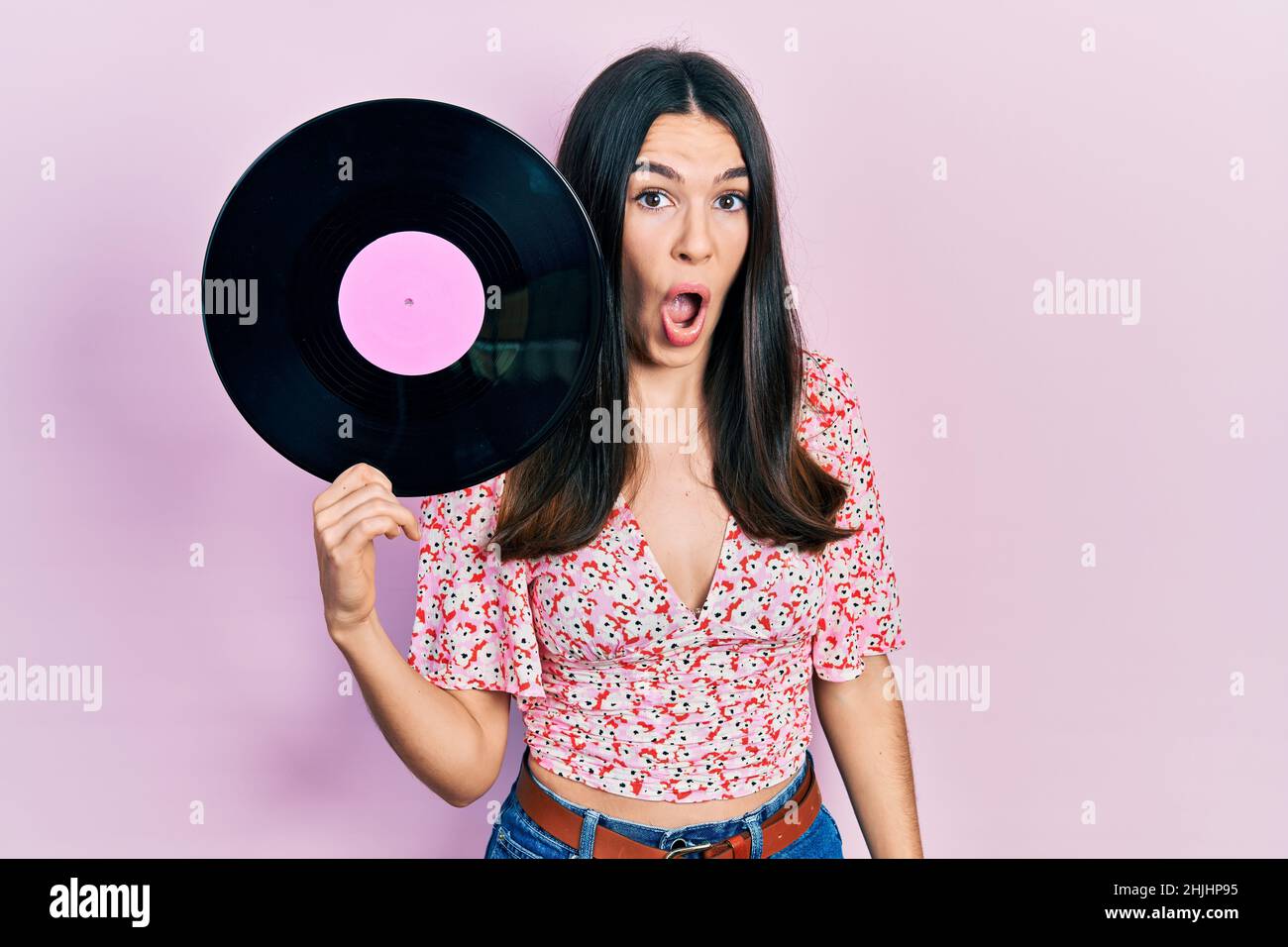 Young brunette woman holding vinyl disc scared and amazed with open ...