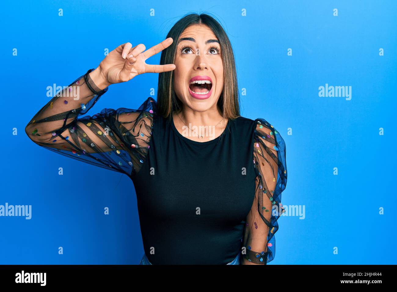 Young hispanic woman with victory gesture fingers on eye angry and mad ...