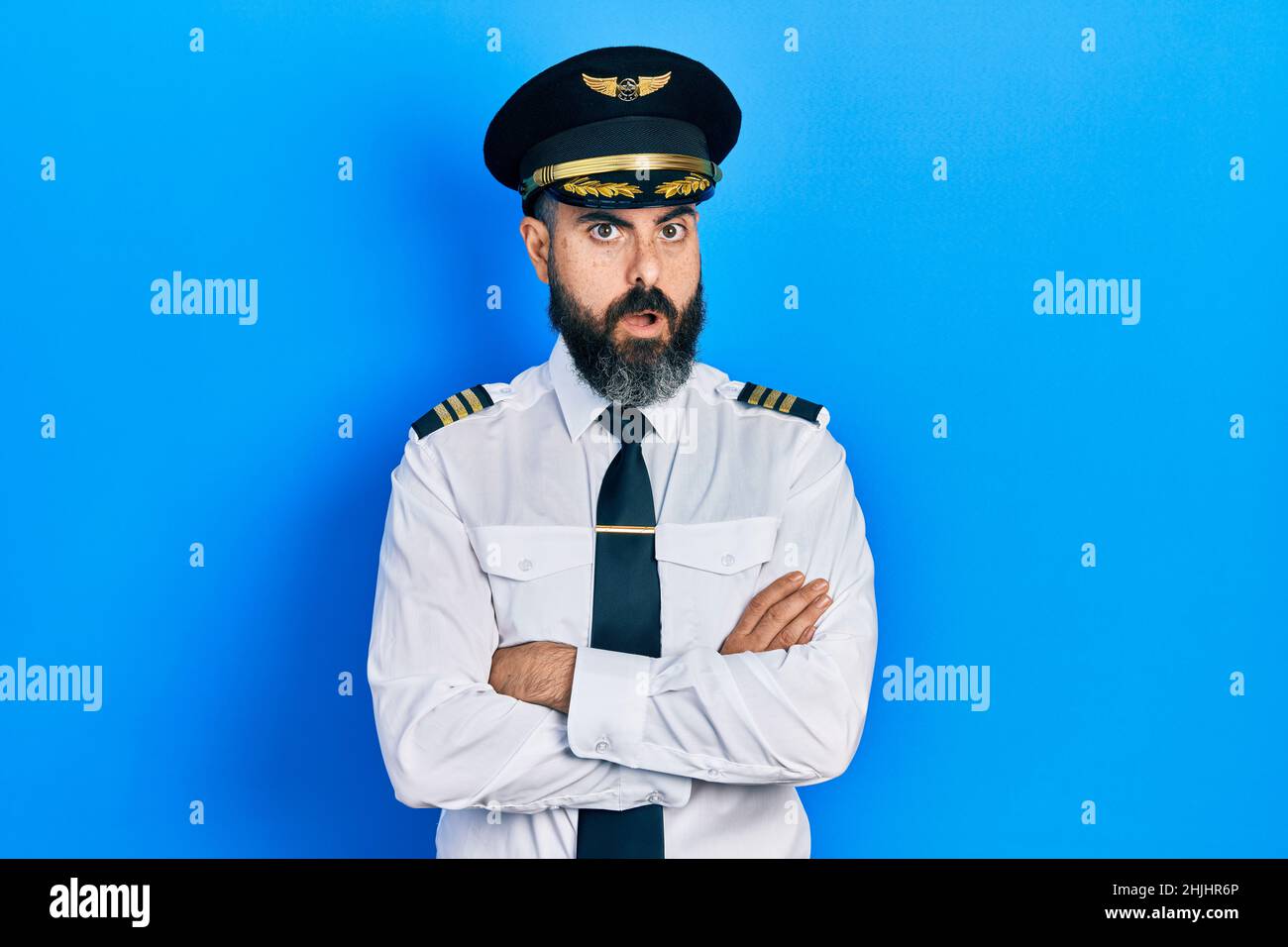 Young hispanic man wearing airplane pilot uniform with arms crossed ...