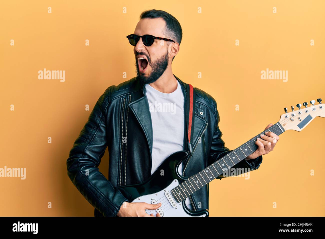 Young man with beard playing electric guitar angry and mad screaming ...