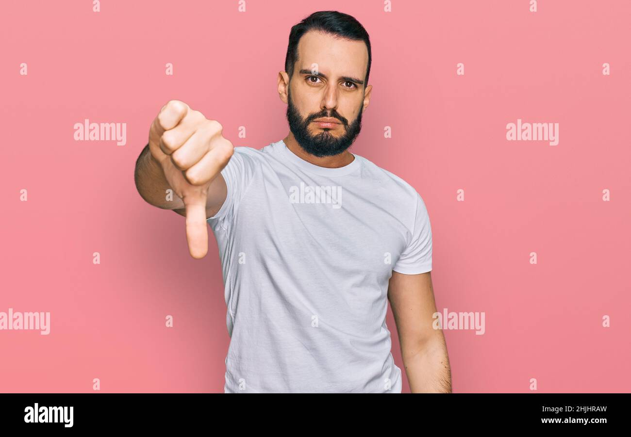 Young man with beard wearing casual white t shirt looking unhappy and ...