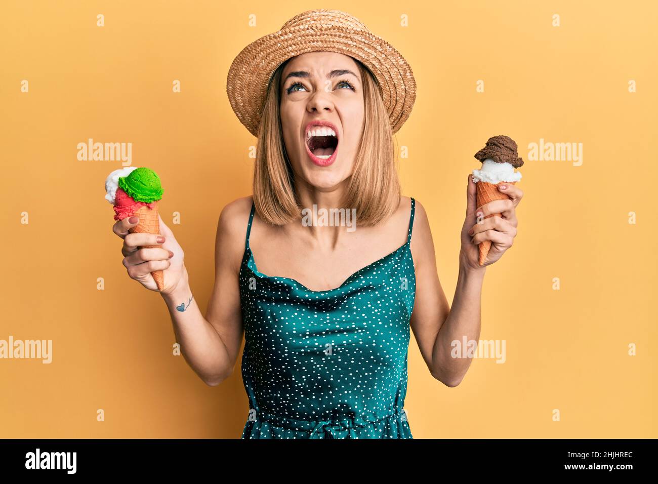 Young caucasian blonde woman eating ice cream cone angry and mad ...