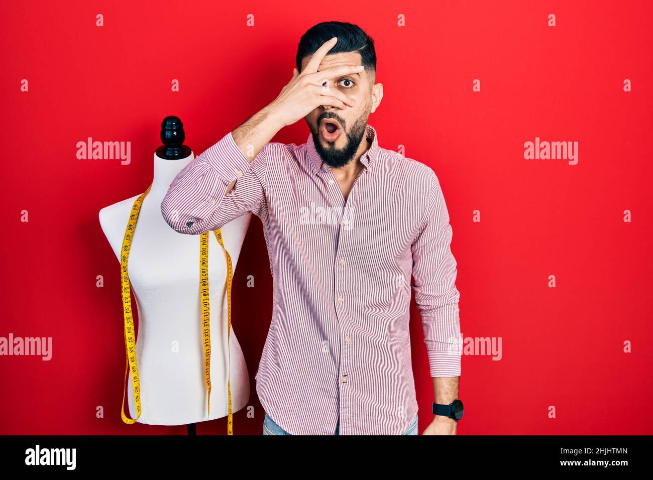 Handsome tailor man with beard standing by manikin peeking in shock ...