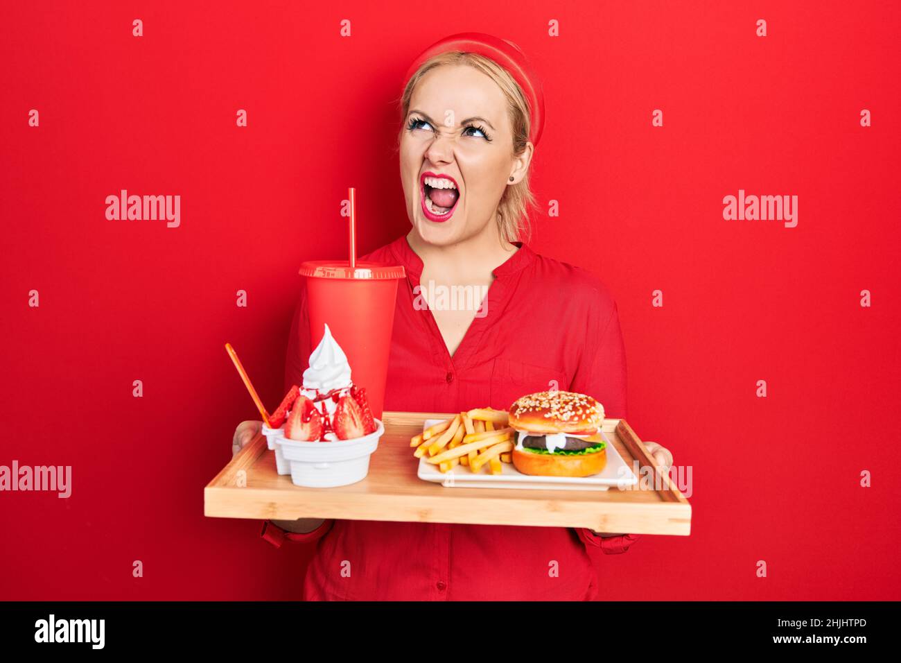 Young blonde woman eating a tasty classic burger with fries and soda ...