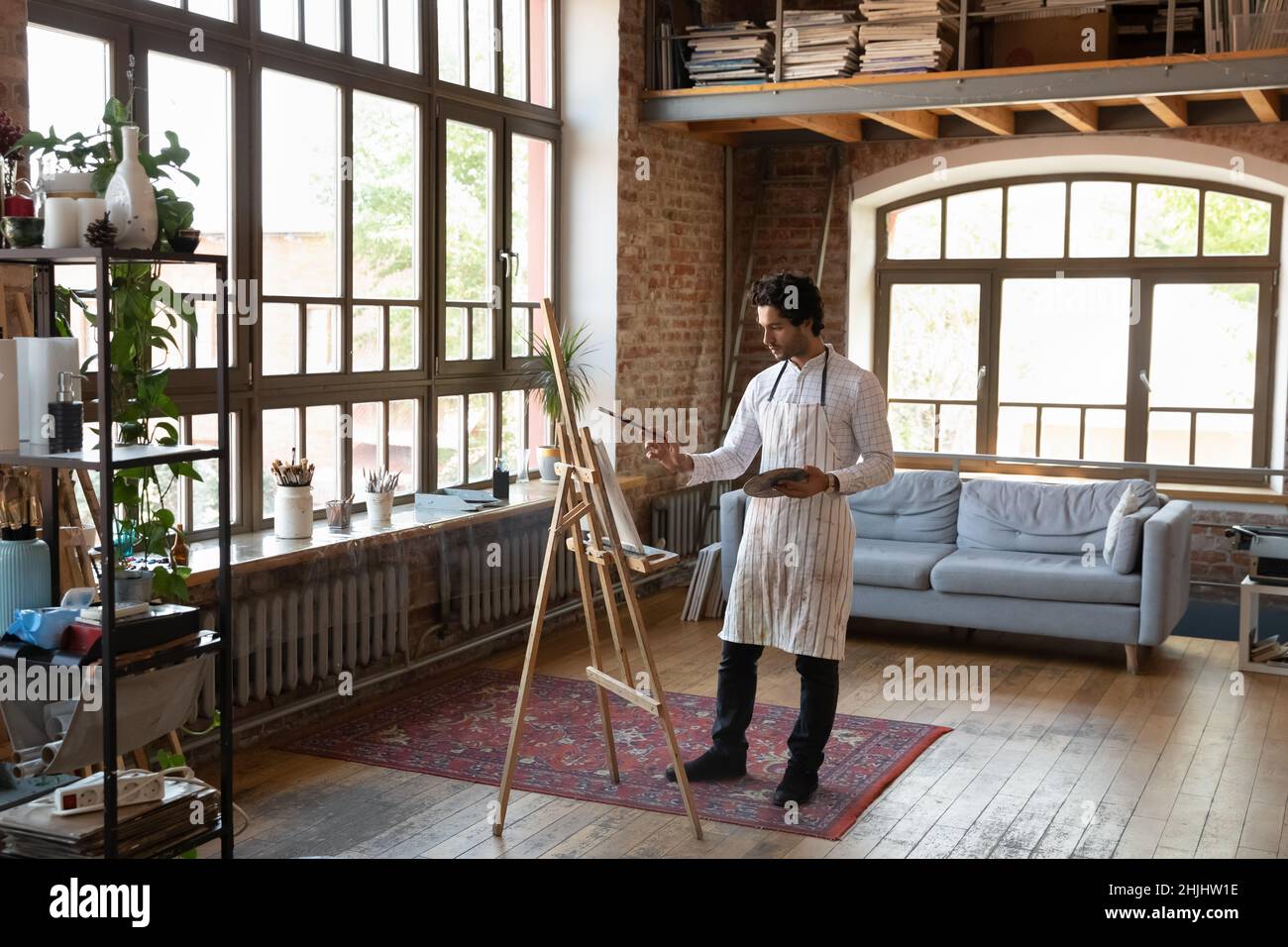 Young male artist working in home studio, standing at easel Stock Photo ...