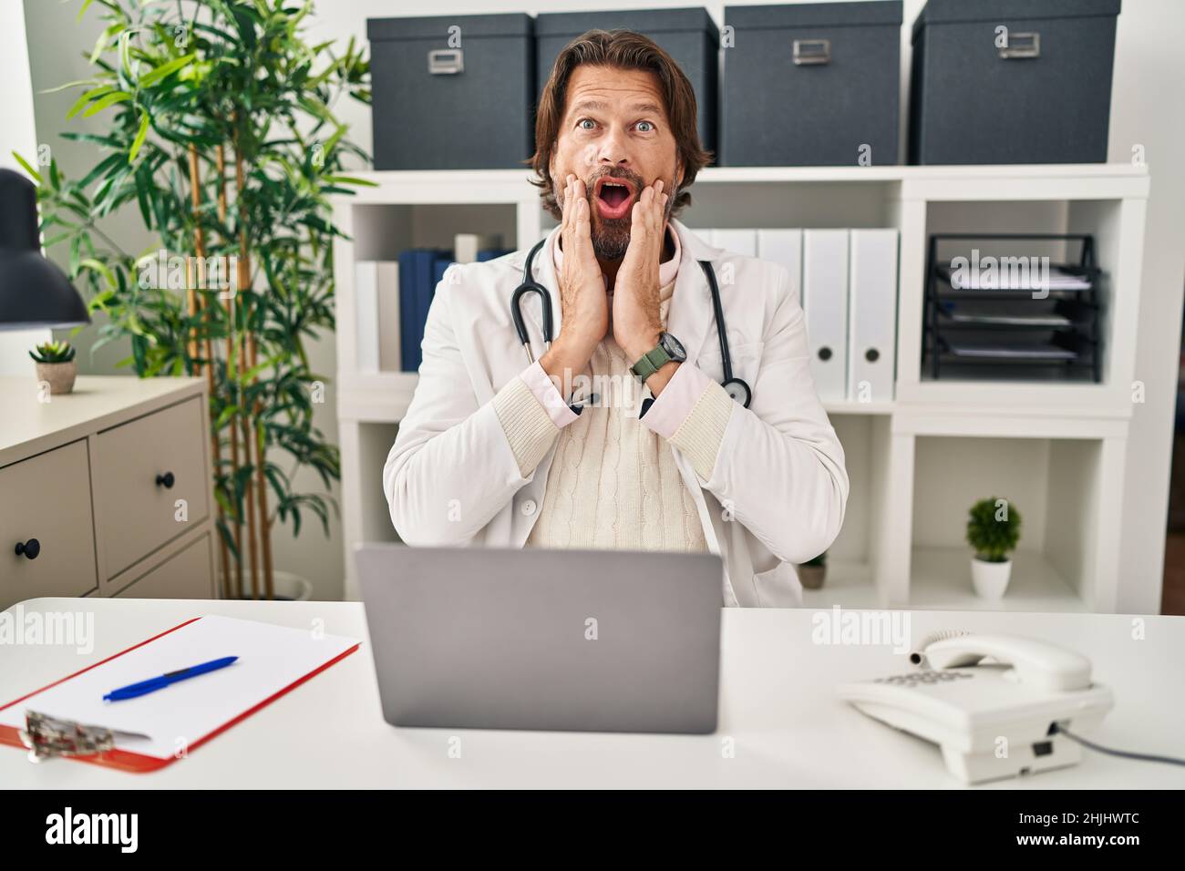 Handsome middle age doctor man working at the clinic afraid and shocked ...