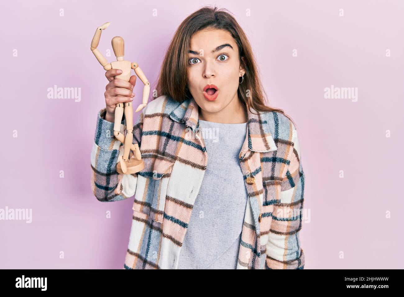 Young caucasian girl holding small wooden manikin scared and amazed ...
