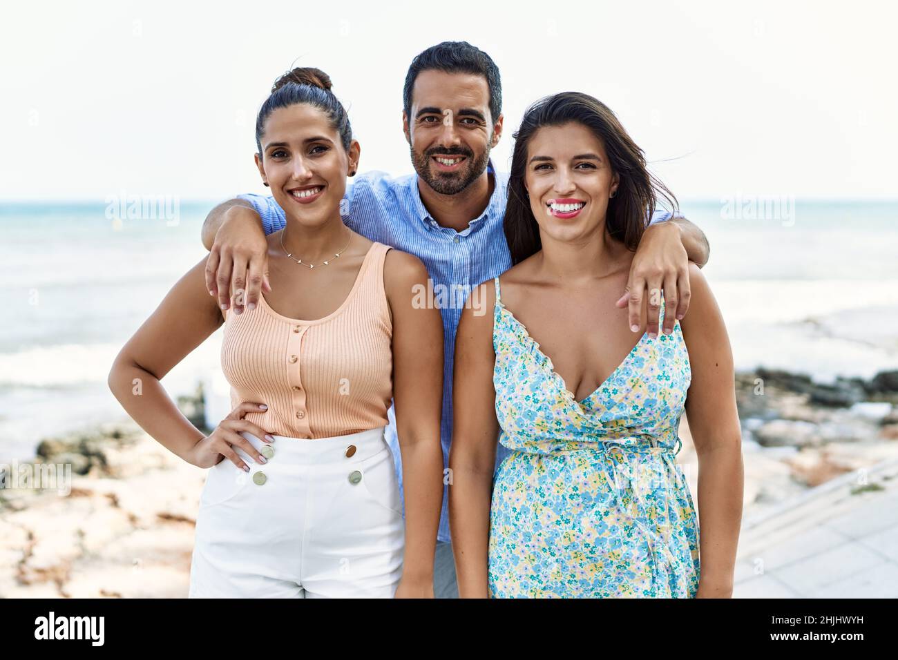 Three young hispanic friends smiling happy and hugging at the beach ...
