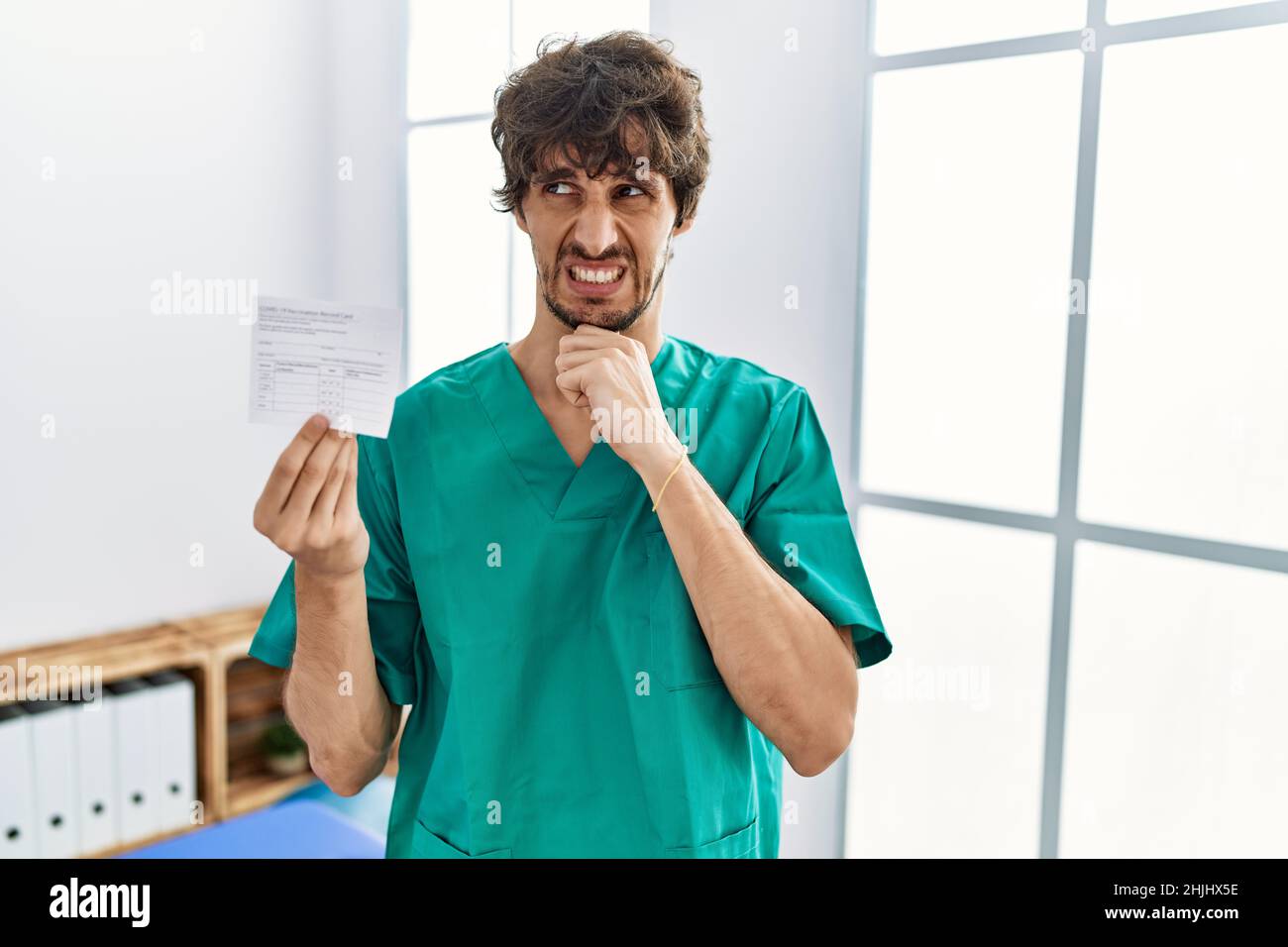 Young hispanic doctor man holding covid record card thinking worried ...