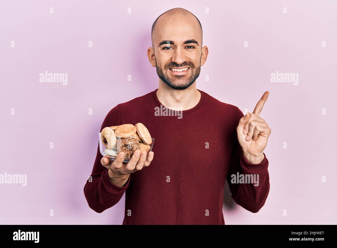 Young bald man holding sweet pastries smiling happy pointing with hand ...