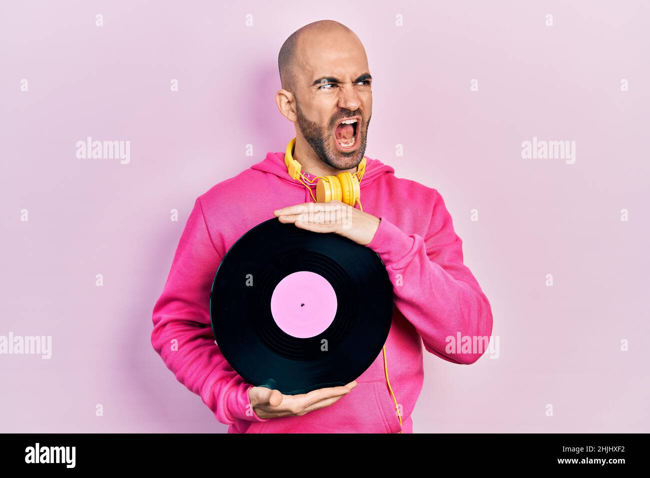 Young bald man holding vinyl disc angry and mad screaming frustrated ...