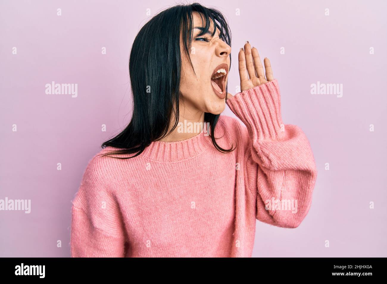 Young brunette woman with bangs wearing casual winter sweater shouting ...