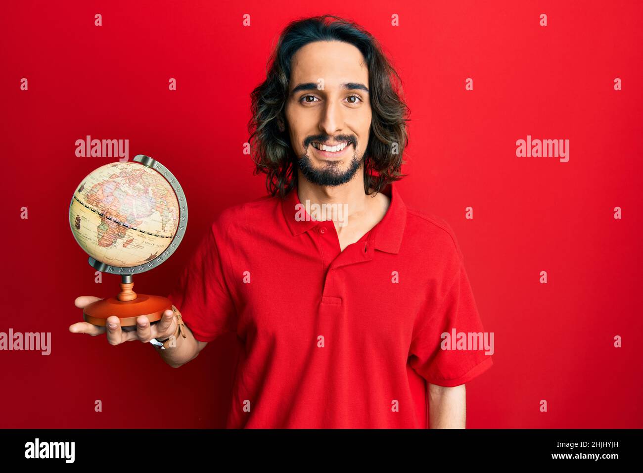 Young hispanic man holding small world ball looking positive and happy ...