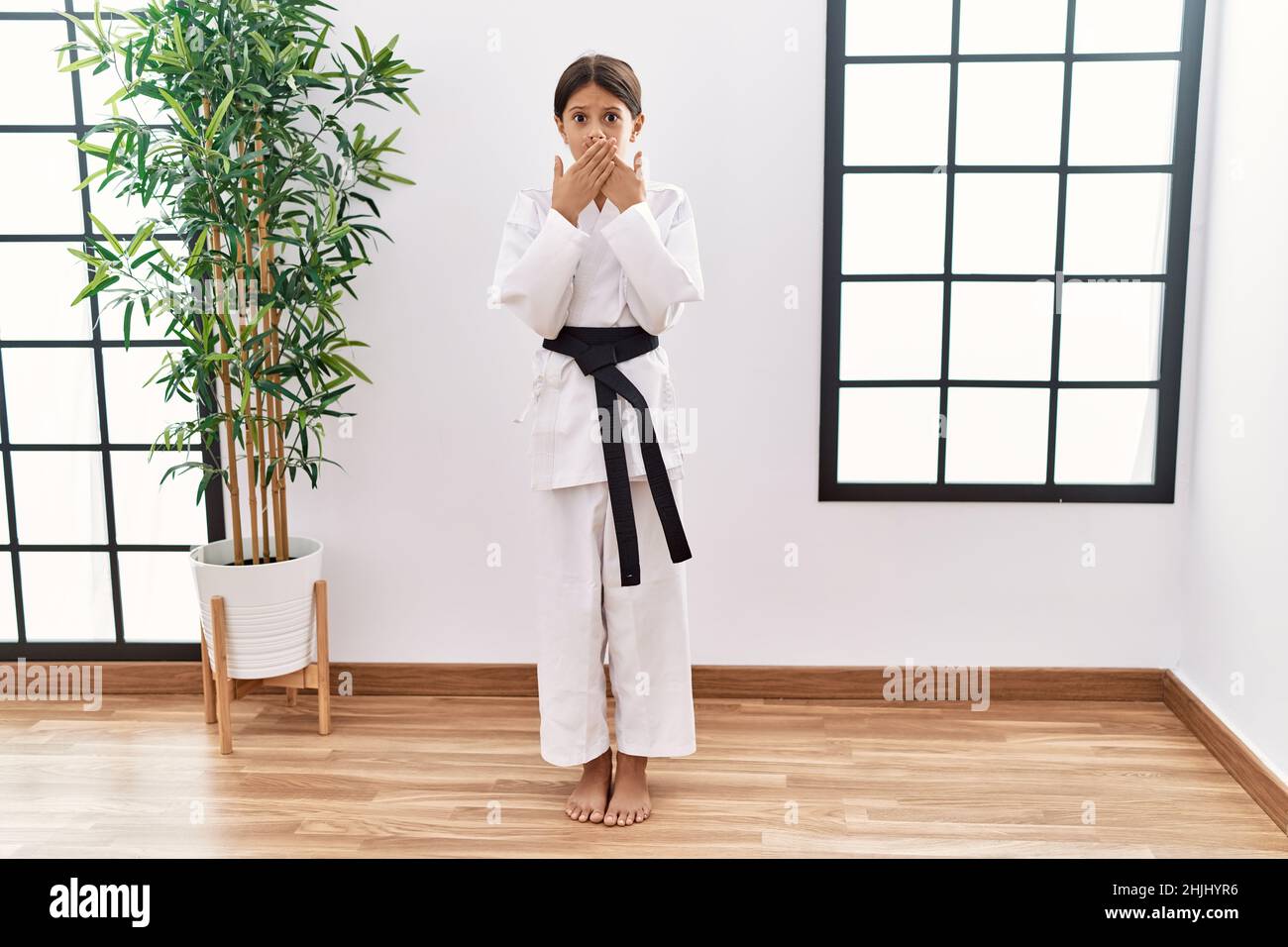 Young hispanic girl wearing karate kimono and black belt shocked ...