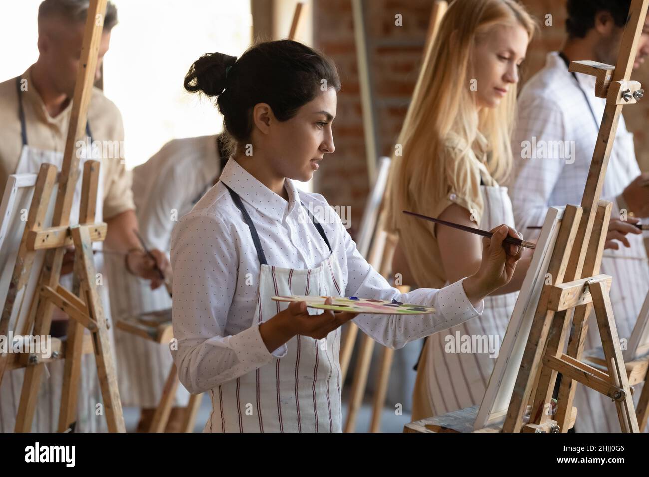 Focused inspired Indian artistic class student girl drawing in paints ...